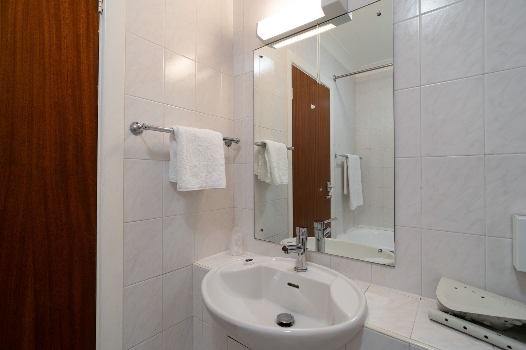 Casa de banho com lavatório branco, espelho, porta-toalhas e porta de madeira.