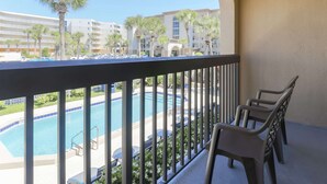 Varanda com vista para a piscina, cadeiras e um edifício ao fundo.