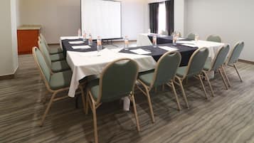 Sala de conferência com grande mesa, cadeiras, tela de projetor e garrafas de água.