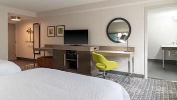 Quarto de hotel com duas camas, uma secretária com computador, televisão, espelho e banheiro.