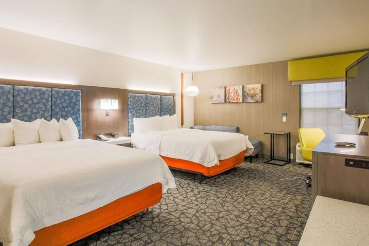 Quarto de hotel com duas camas, uma escrivaninha, uma cadeira e uma televisão.