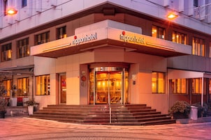Entrada de hotel com porta de vidro, degraus que a levam e um letreiro acima da porta.