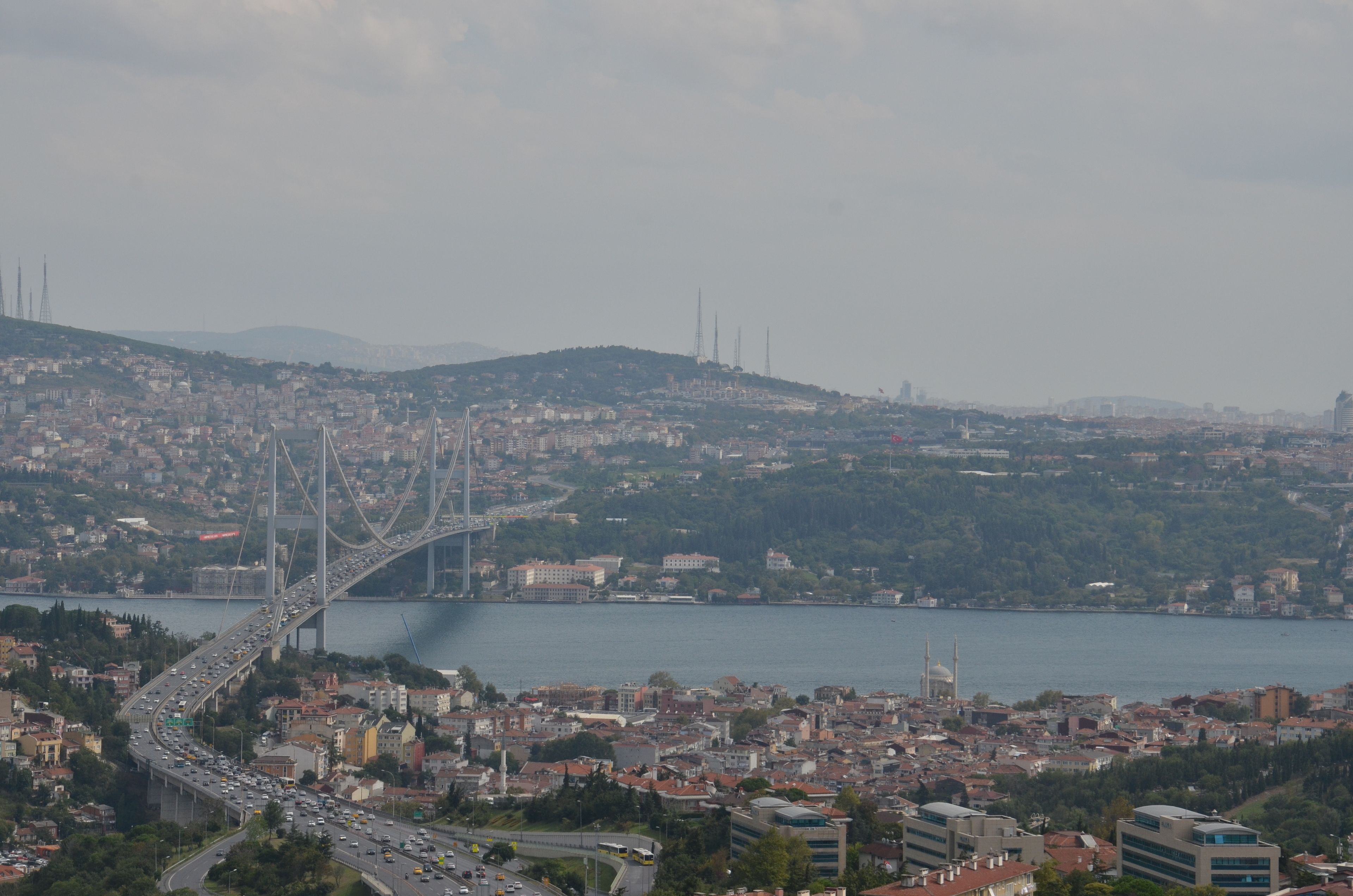Paisagem urbana com uma ponte imponente atravessando um corpo de água, cercada por intenso desenvolvimento urbano e colinas.