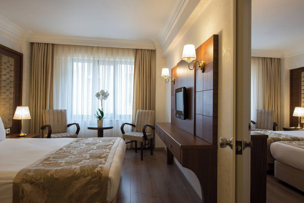 Quarto de hotel com uma cama grande, uma escrivaninha, duas cadeiras, uma televisão e uma orquídea em vaso.