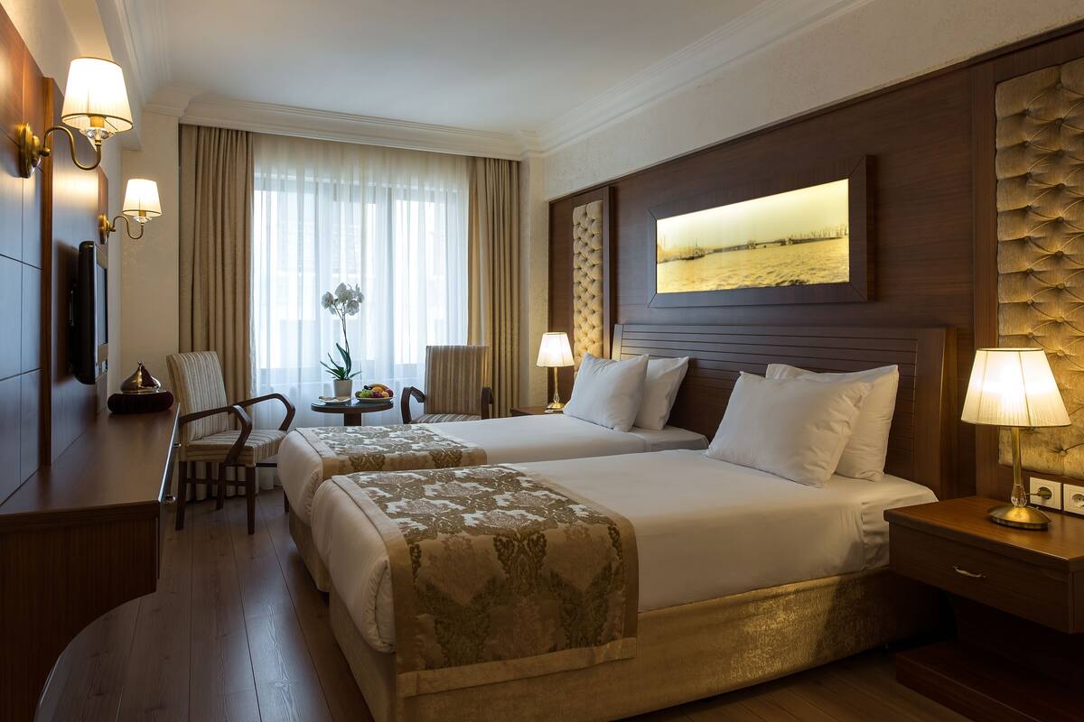Quarto de hotel com duas camas, uma escrivaninha, uma cadeira, uma televisão e uma janela com cortinas.