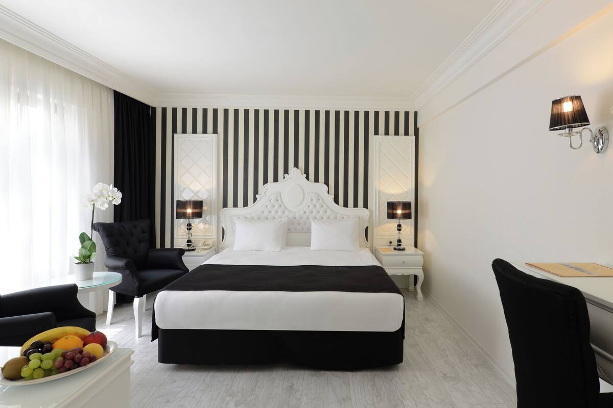 Quarto de hotel com uma cama grande, uma escrivaninha, uma cadeira, uma mesa de cabeceira e um espelho.