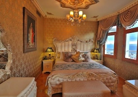 Quarto luxuoso com uma cama grande, cabeceira decorada e um candelabro.