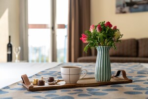 Uma bandeja com uma xícara de café, um vaso de flores e alguns chocolates sobre uma toalha de mesa estampada.