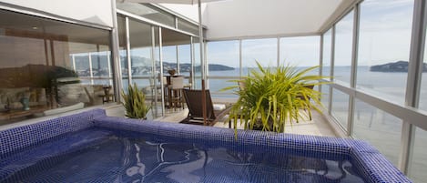 Piscina interior moderna com vista para o mar e área de varanda com assentos e plantas.