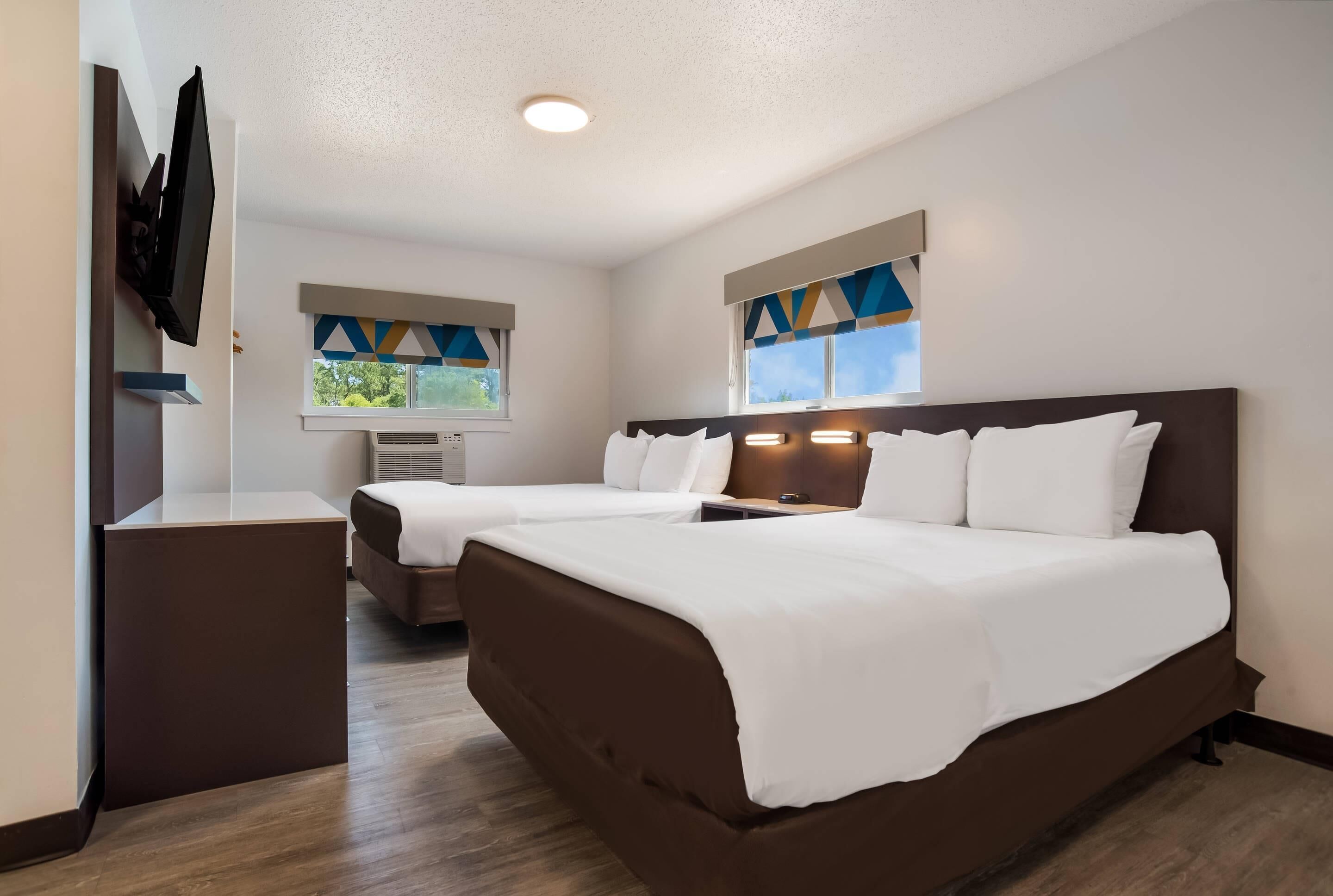 Quarto de hotel com duas camas, televisão de tela plana, escrivaninha e janela com vista.