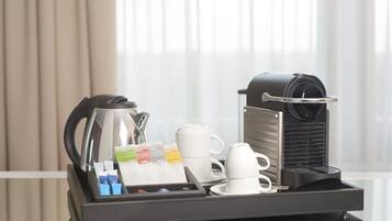Uma estação de café com cafeteira, xícaras e uma bandeja de cápsulas de café.
