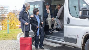Uma carrinha branca com a inscrição 'hotel shuttle' e '24/7' na lateral, indicando que é utilizada para serviços de transporte do hotel.