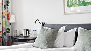 Uma cama bem arrumada com almofadas estampadas, uma mesinha de cabeceira com abajur e um quadro na parede.