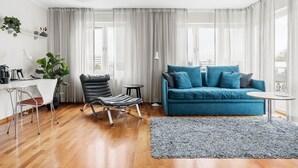 Uma sala de estar moderna com um sofá azul, um tapete cinza e uma área de jantar com uma mesa e cadeiras brancas.