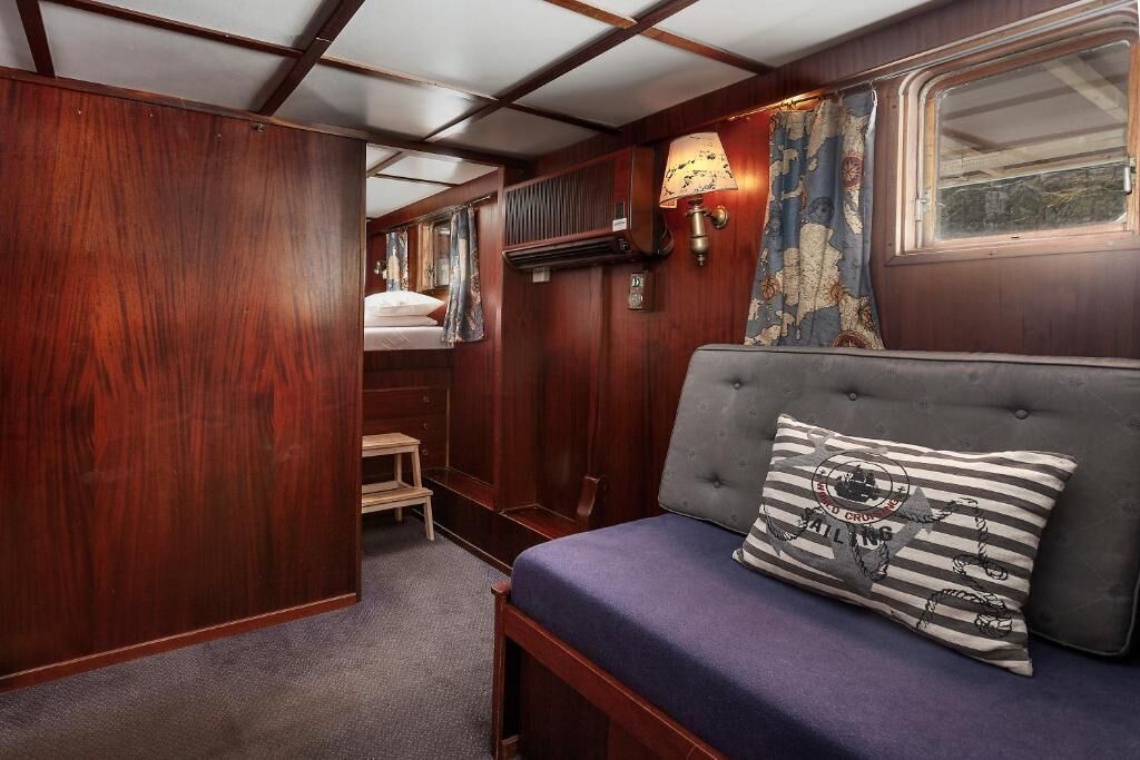 Uma cabana acolhedora com interior de madeira, um banco estofado, uma mesa pequena e uma janela com cortinas.