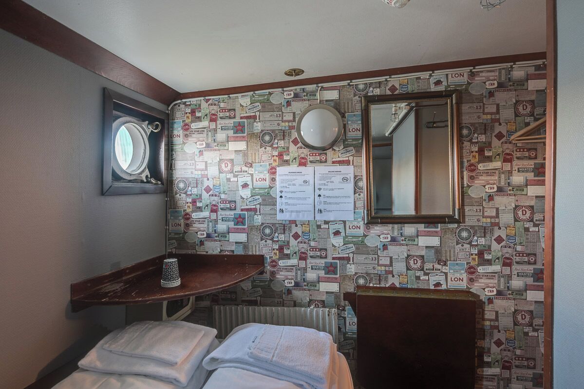 Quarto com parede estampada, espelho redondo, mesa pequena e radiador.
