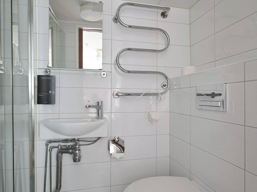 Casa de banho moderna com cabine de duche em vidro, lavatório branco, sanita e barra de apoio.