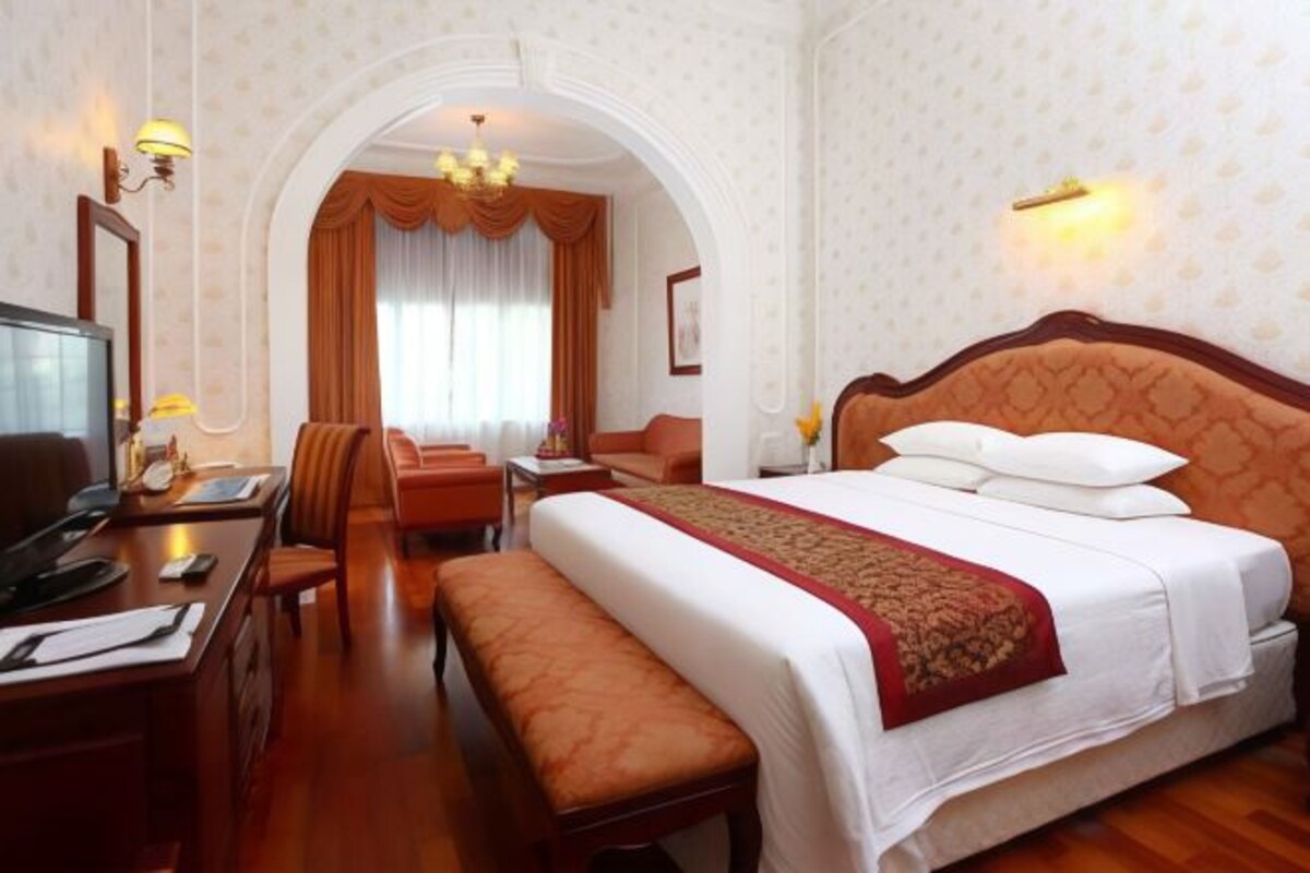 Quarto de hotel com uma cama grande, uma mesa com computador, uma cadeira e um banco.