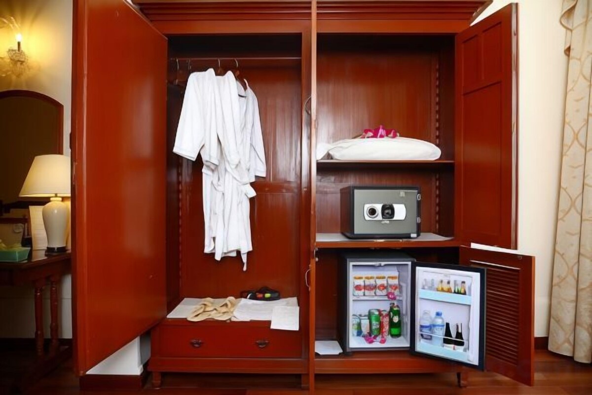 Um guarda-roupa de madeira com um roupão branco pendurado, um pequeno frigorífico com bebidas e um micro-ondas.