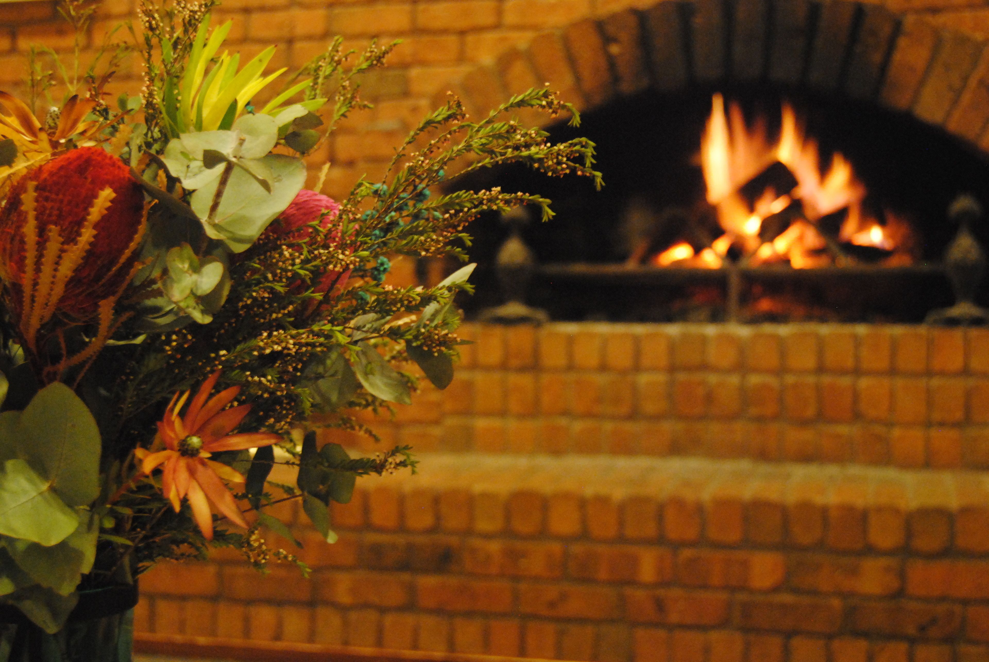 Lareira de tijolos com fogo e um arranjo floral em primeiro plano.