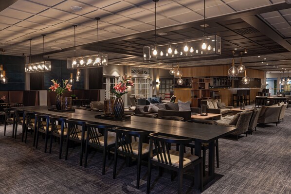Um restaurante moderno com uma mesa comunitária grande, várias áreas de estar e luminárias pendentes.