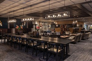 Um restaurante moderno com uma mesa comunitária grande, várias áreas de estar e luminárias pendentes.