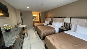 Quarto de hotel com duas camas, uma escrivaninha, uma cadeira, uma televisão e um banheiro visível por uma porta aberta.