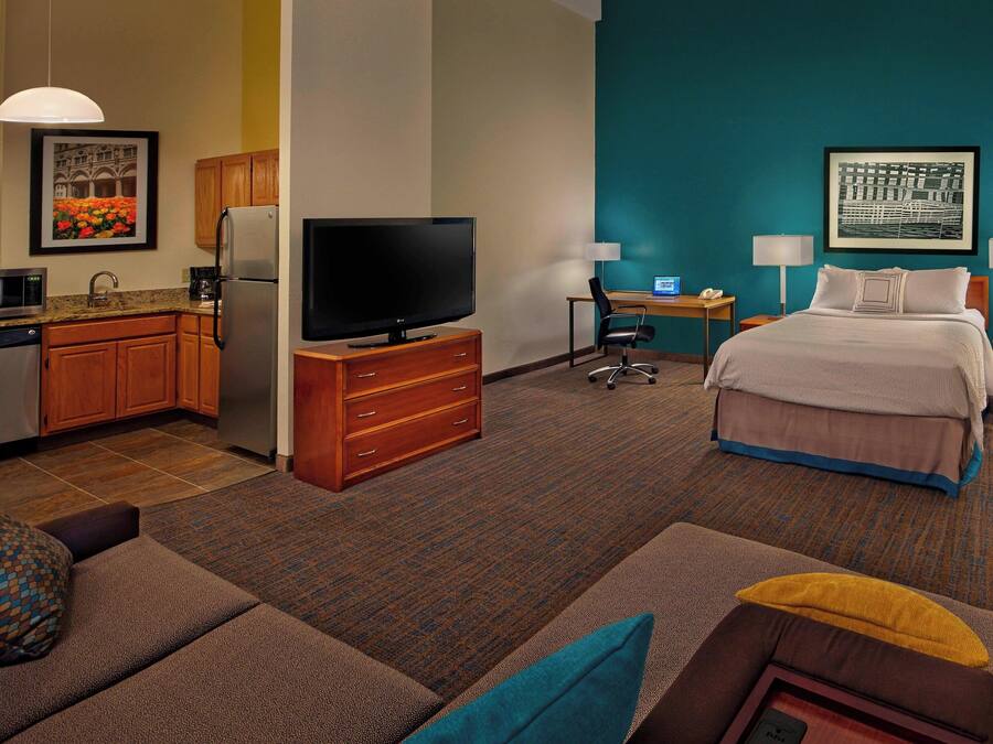 Quarto de hotel com cozinha compacta, cama, escrivaninha e televisão.
