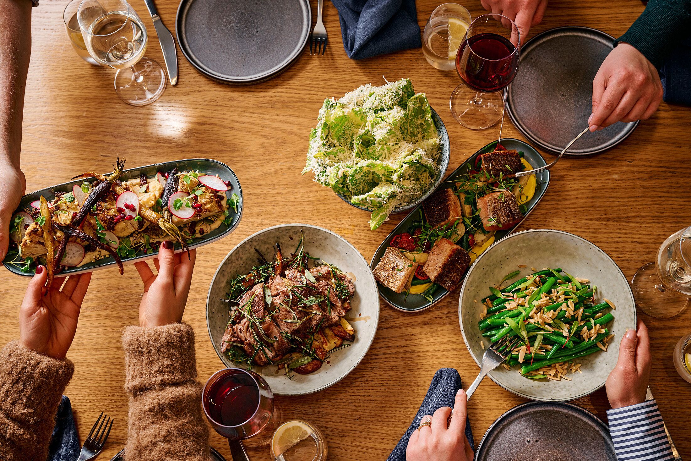 Uma mesa de jantar com vários pratos, incluindo um prato de carne assada, uma tigela de legumes verdes e um prato de pão.