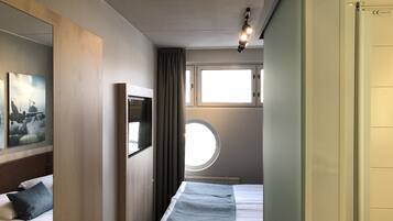 Quarto de hotel com cama, mesa de cabeceira, espelho, janela e luminária no teto.