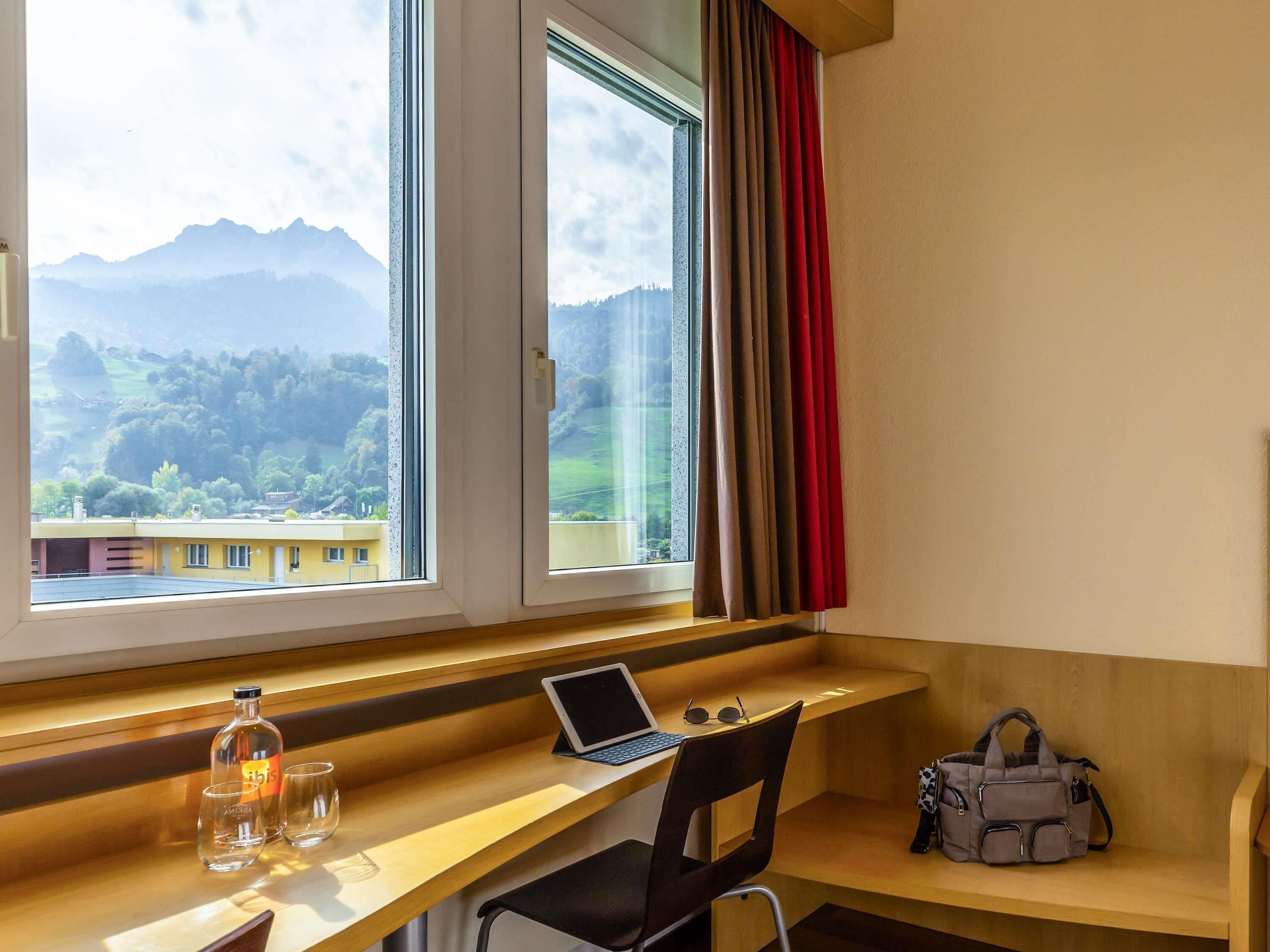 Quarto com escrivaninha de madeira, um laptop, uma garrafa e copos.