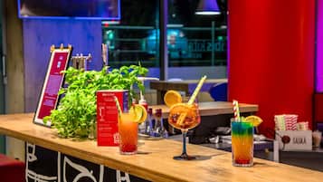 Uma área de bar com um cardápio, um vaso de planta e três coquetéis coloridos no balcão.