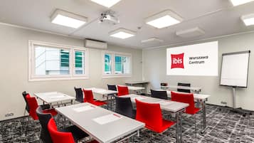 Uma sala de conferências com mesas, cadeiras, uma tela de projetor e um quadro branco.