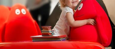 Uma criança sentada em uma cadeira vermelha com uma pilha de livros ao lado.