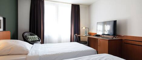 Quarto de hotel com duas camas, uma escrivaninha, uma cadeira, televisão e janela com cortinas.