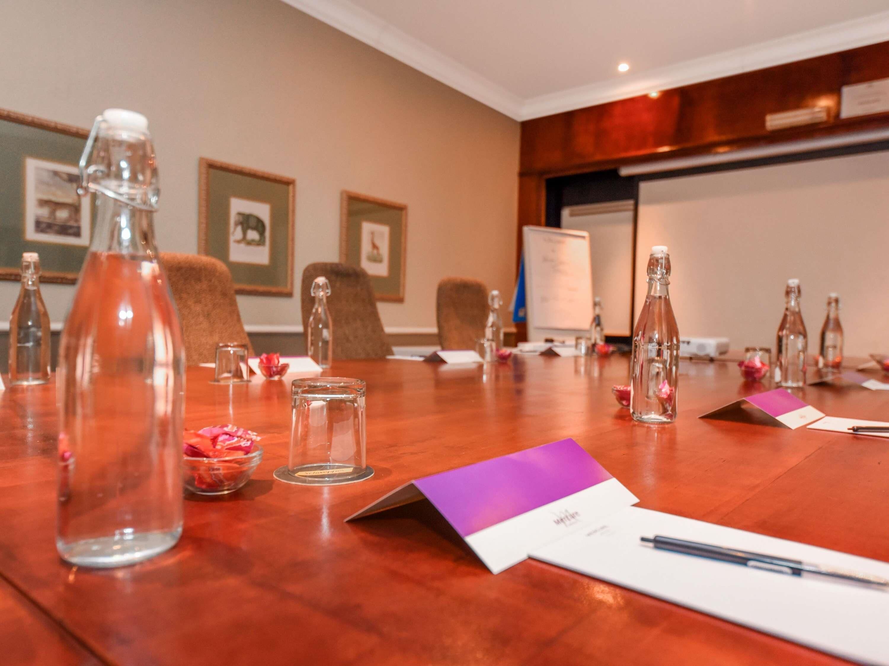 Uma sala de conferências com uma mesa de madeira, garrafas de vidro transparente, um quadro branco e quadros nas paredes.
