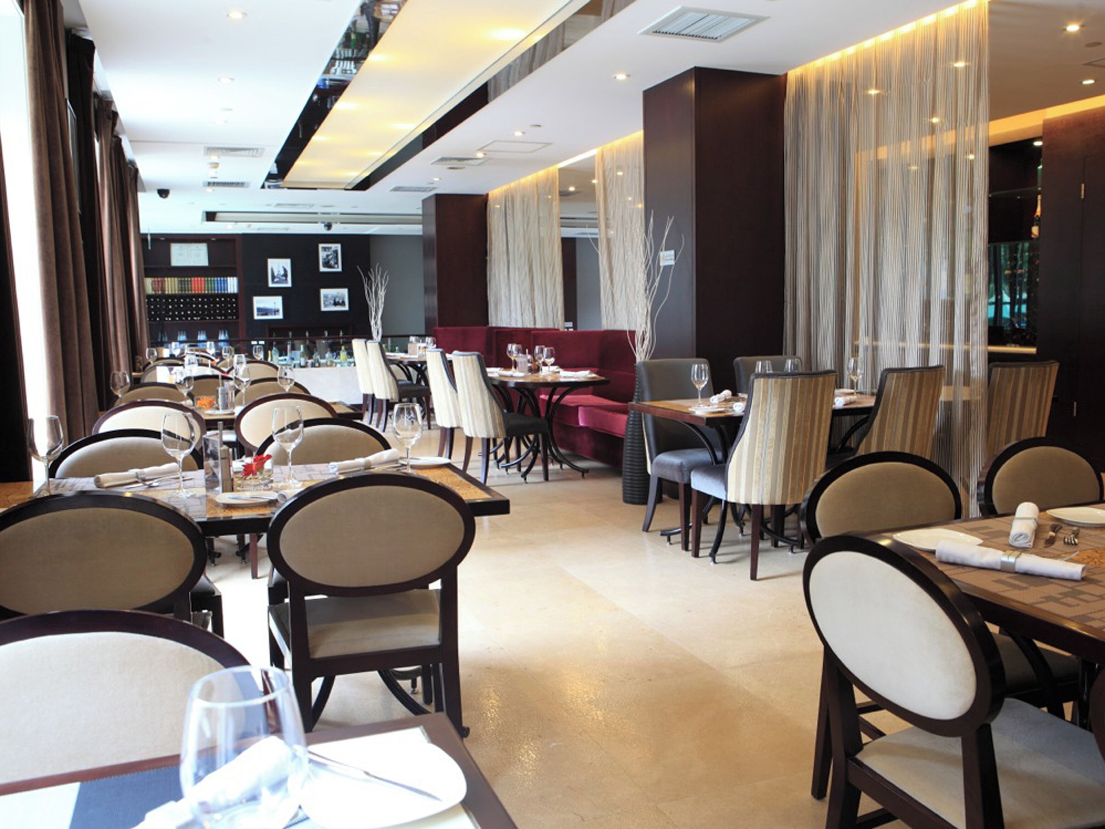 Espaço de refeições moderno com mesas e cadeiras, um bar ao fundo e vista para a cidade.