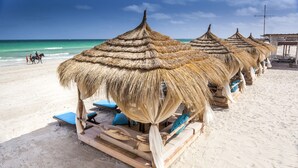 Uma praia com guarda-sóis de palha e espreguiçadeiras.