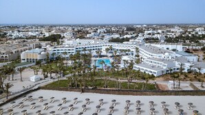 Um resort com uma piscina grande, vários edifícios brancos e inúmeras espreguiçadeiras dispostas em fileiras.