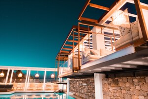 Uma área moderna de piscina ao ar livre, com muro de pedra, espreguiçadeiras e escadaria que dá acesso a uma varanda com vista para o céu noturno.
