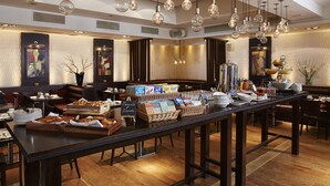 Uma sala de jantar de hotel com uma longa mesa posta para o pequeno-almoço, apresentando várias opções de comida e uma estação de café.