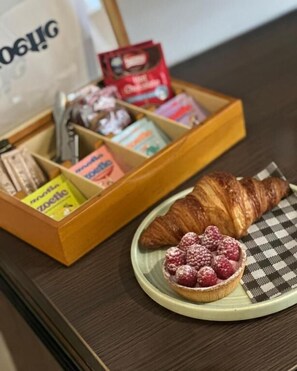 Uma caixa de madeira com diversos alimentos e um croissant com framboesas em um prato.
