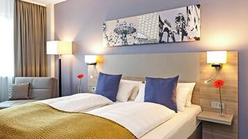 Quarto de hotel com cama de casal, duas mesas de cabeceira com abajures, uma obra de arte na parede e vista para a paisagem urbana pela janela.