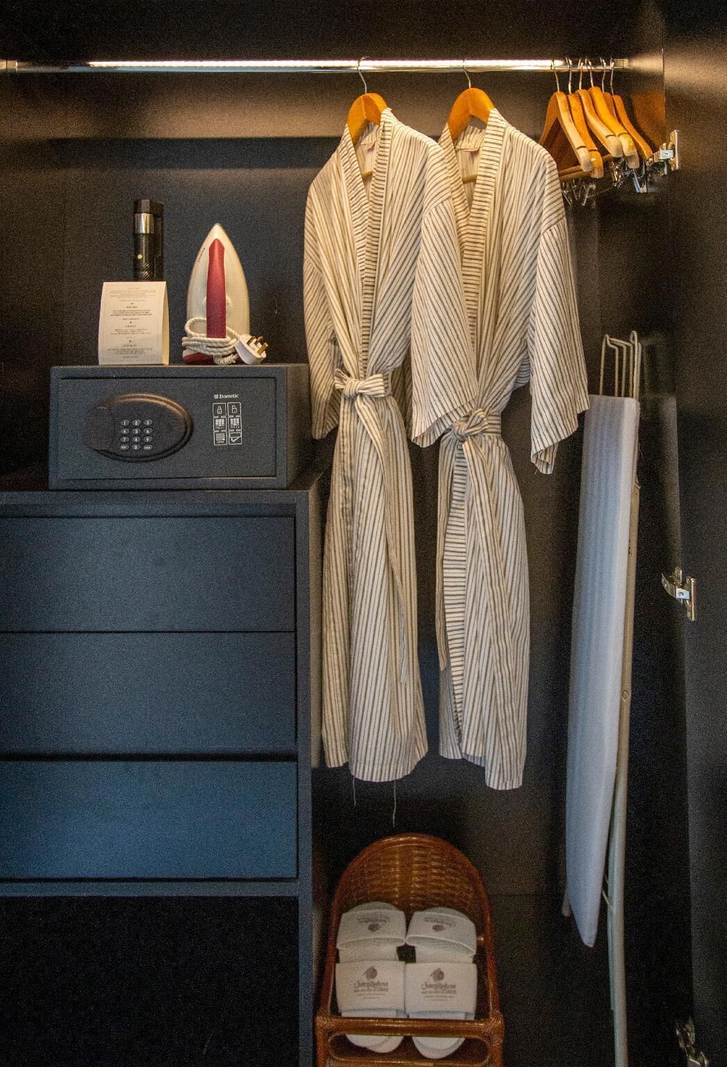 Uma casa de banho de hotel com roupões listrados pendurados num porta-roupões, um chuveiro, um suporte para toalhas e um armário com artigos de higiene pessoal.