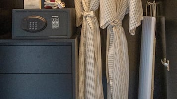 Uma casa de banho de hotel com roupões listrados pendurados num porta-roupões, um chuveiro, um suporte para toalhas e um armário com artigos de higiene pessoal.