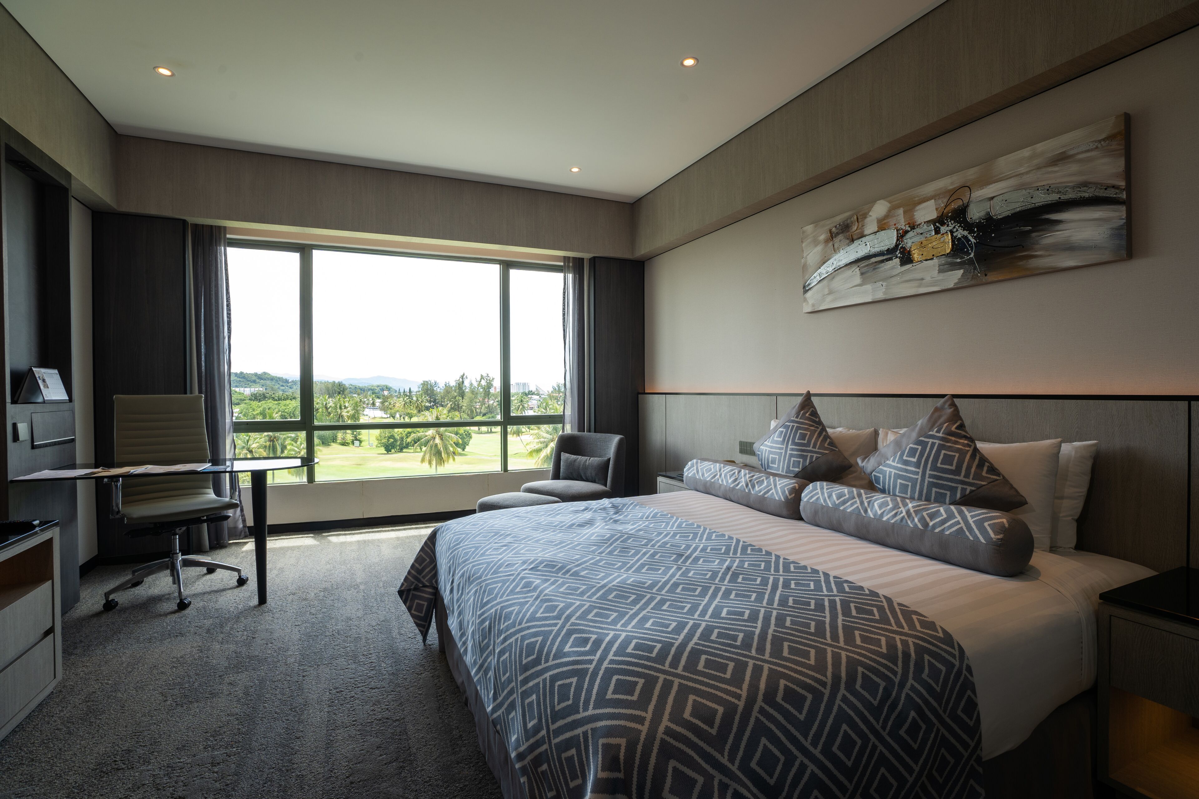 Quarto de hotel moderno com uma cama grande, uma escrivaninha e uma cadeira. Há uma janela ampla que oferece vista para o exterior.