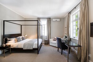 Quarto com cama de dossel, mesas de cabeceira, escrivaninha e uma cadeira.