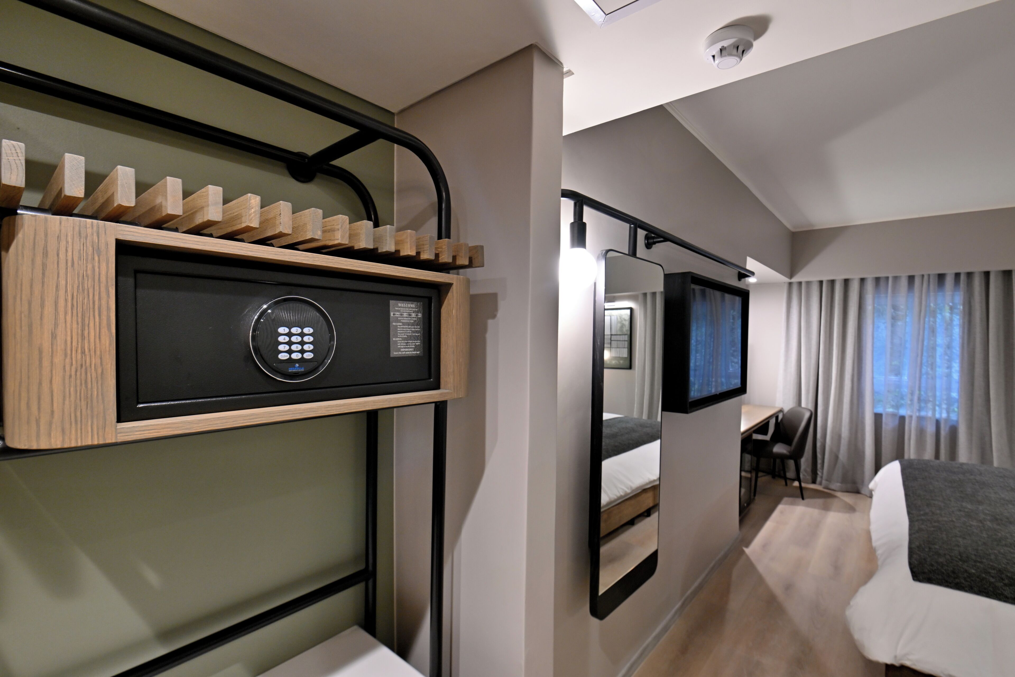 Quarto de hotel moderno com cama, escrivaninha, cadeira, televisão e câmera de segurança.