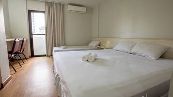 Quarto de hotel com uma cama grande, duas mesas de cabeceira, uma escrivaninha com cadeiras e um ar condicionado.