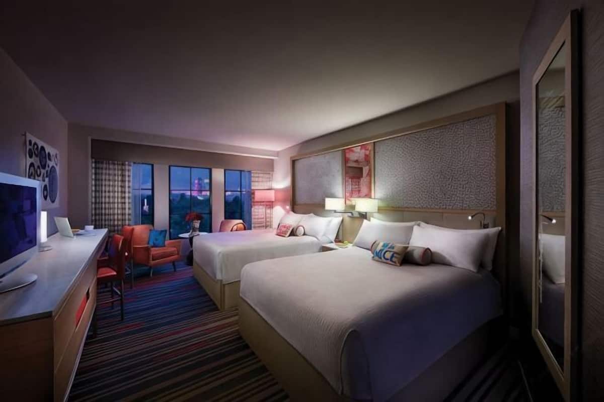 Quarto de hotel com duas camas, uma escrivaninha, televisão e vista para a cidade.